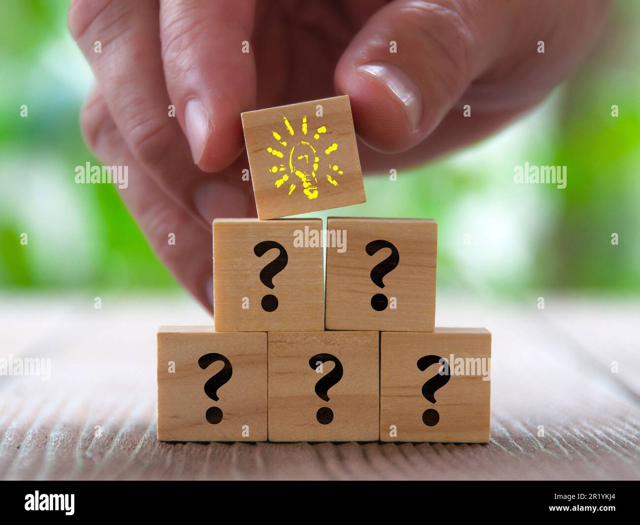 Hand placing wooden cube with yellow color light bulb on top of other ...