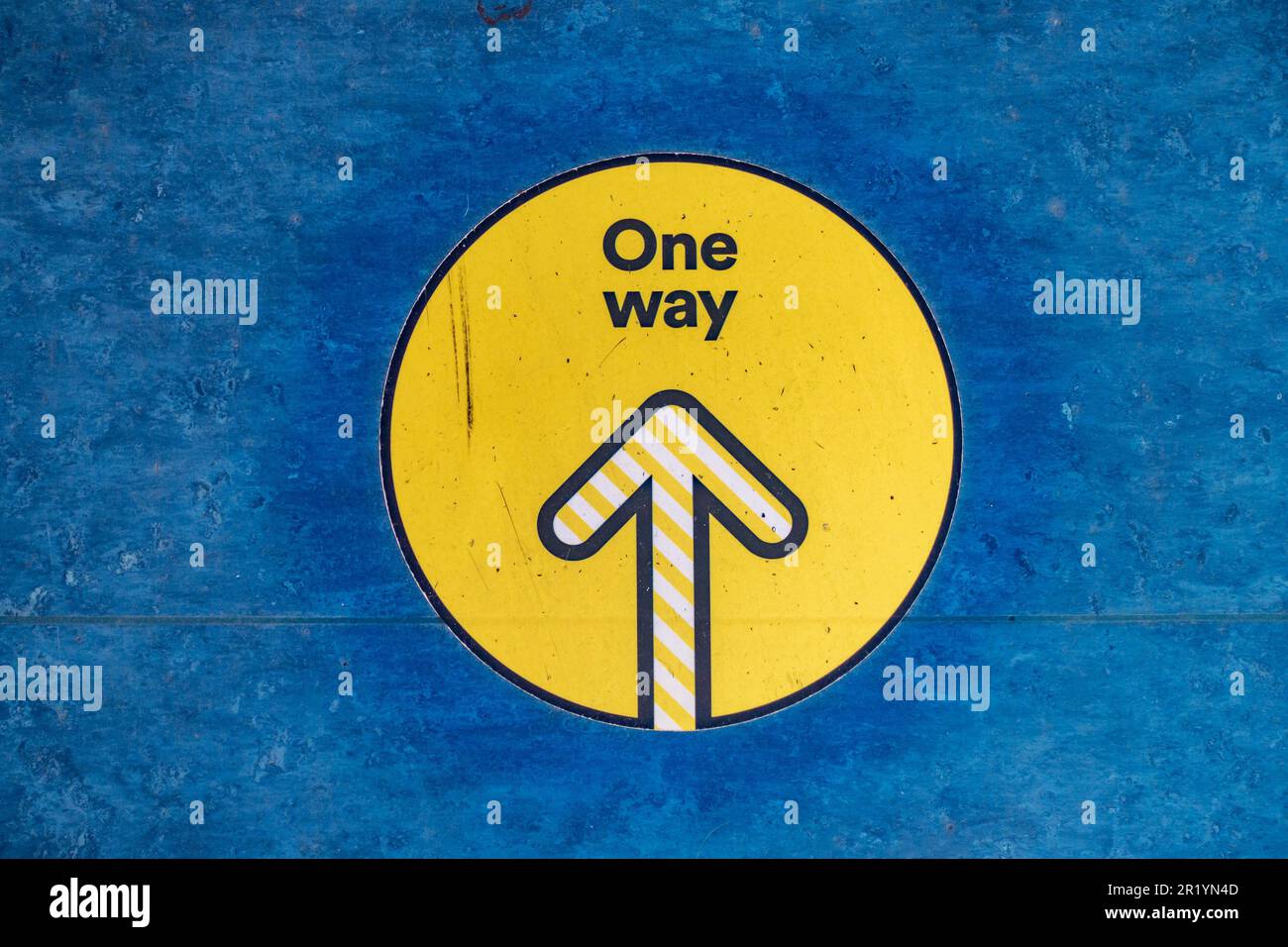 A sign on a floor indicating a one-way system along a corridor, a ...