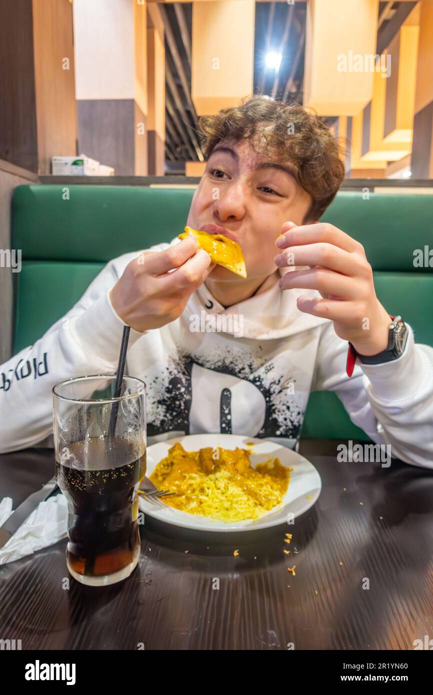 A teenage boy eating curry, rice and naan bread at an asian buffet food ...