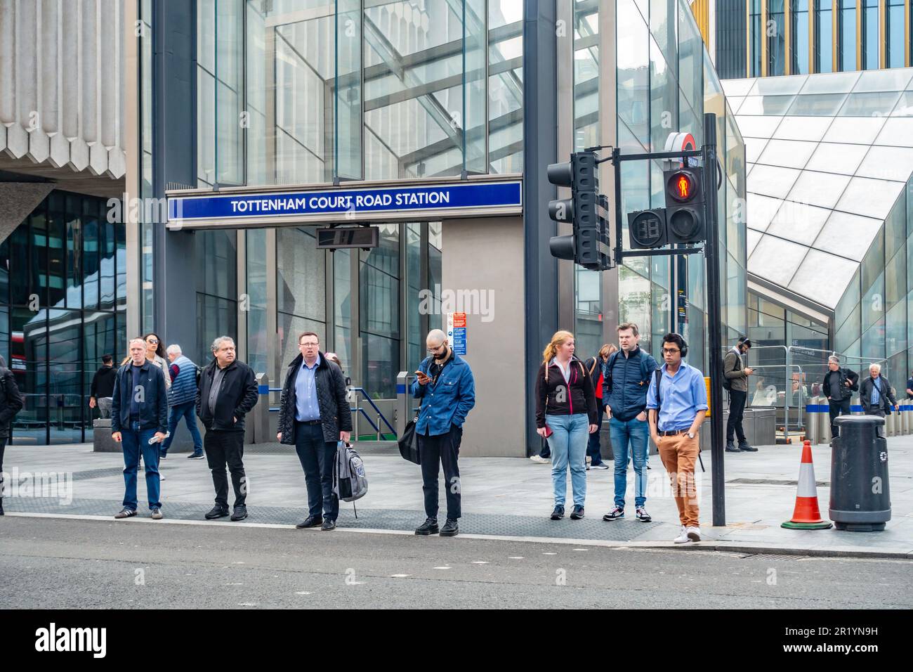 People stand and wait at a pedestrian crossing to cross the road ...