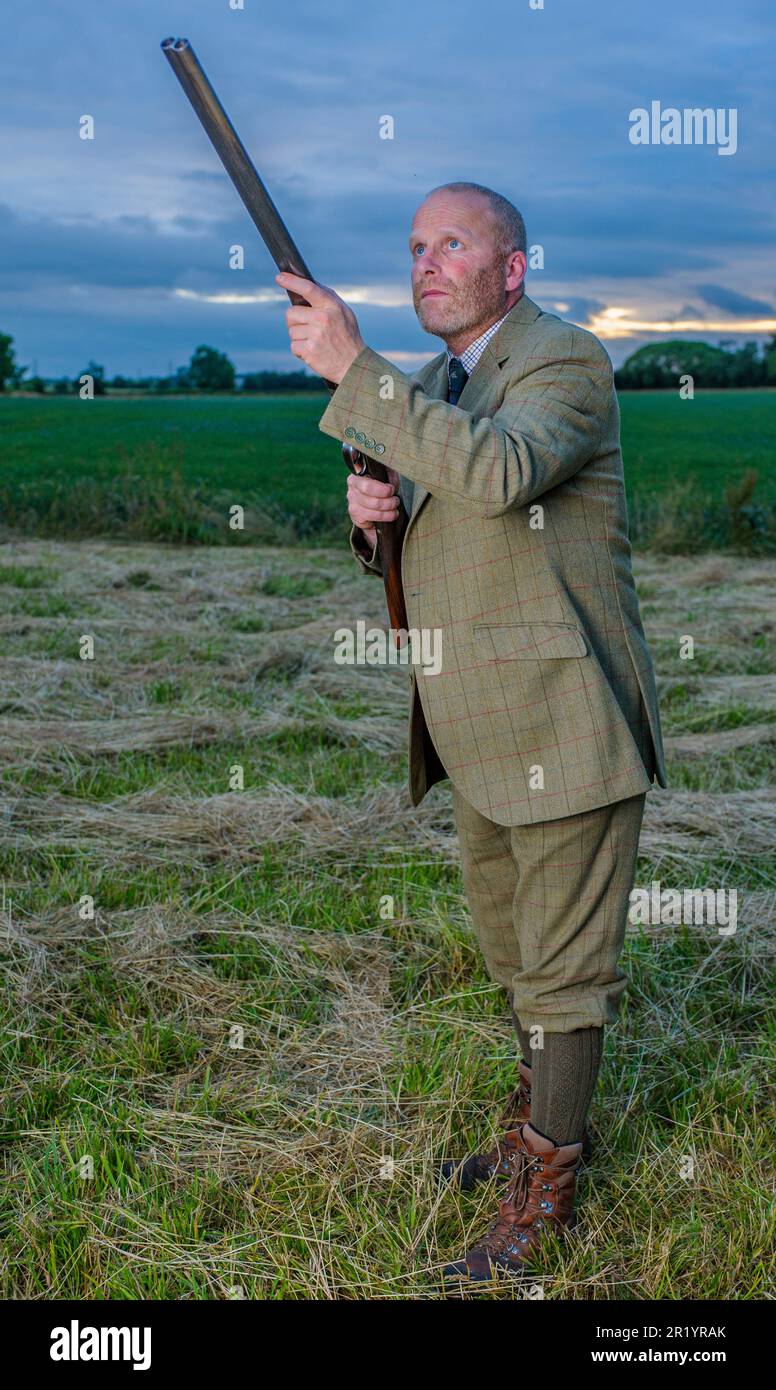 An English gentleman stood at twilight in a tweed shooting suit with a ...