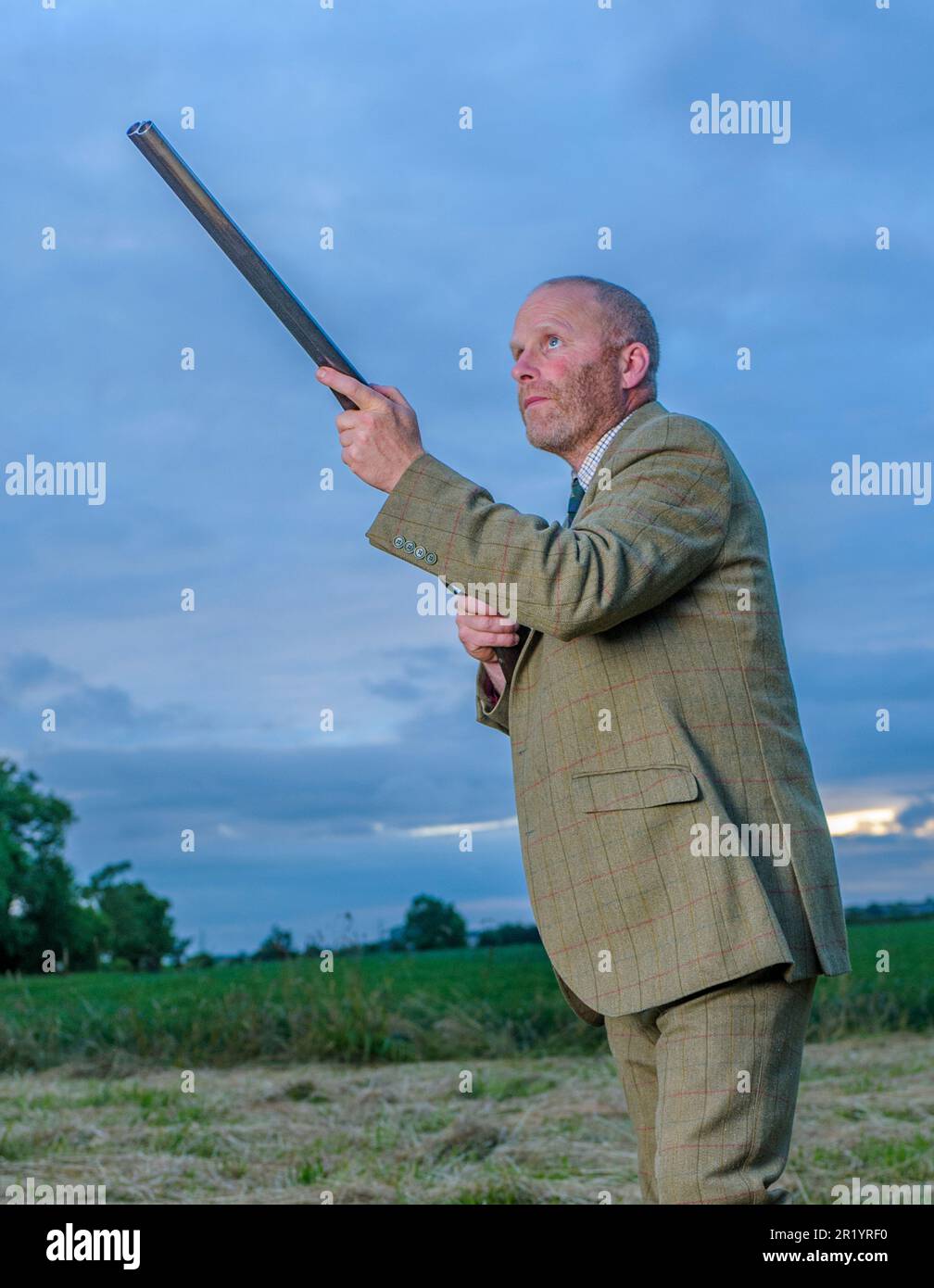 An English gentleman stood at twilight in a tweed shooting suit with a ...