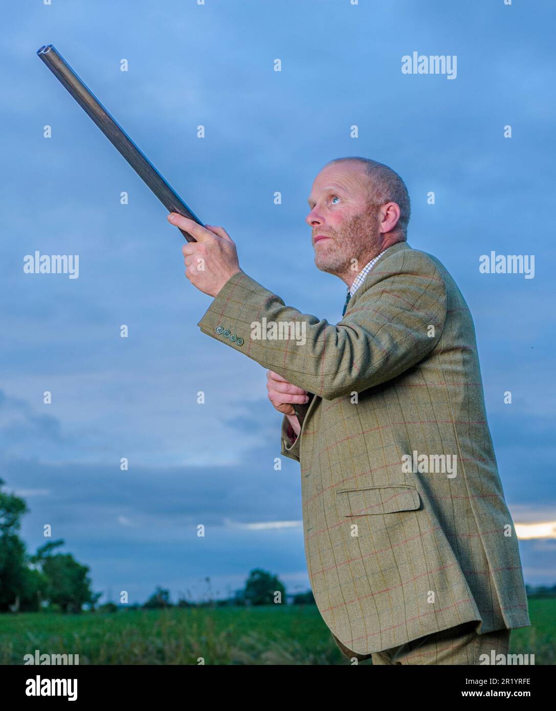 An English gentleman stood at twilight in a tweed shooting suit with a ...