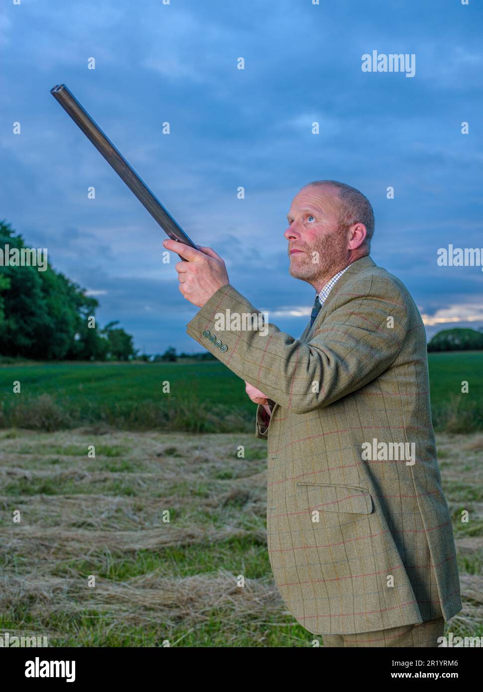An English gentleman stood at twilight in a tweed shooting suit with a ...