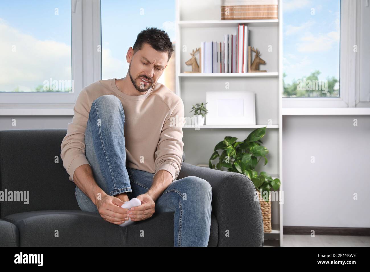 Man suffering from foot pain on sofa at home, space for text Stock ...