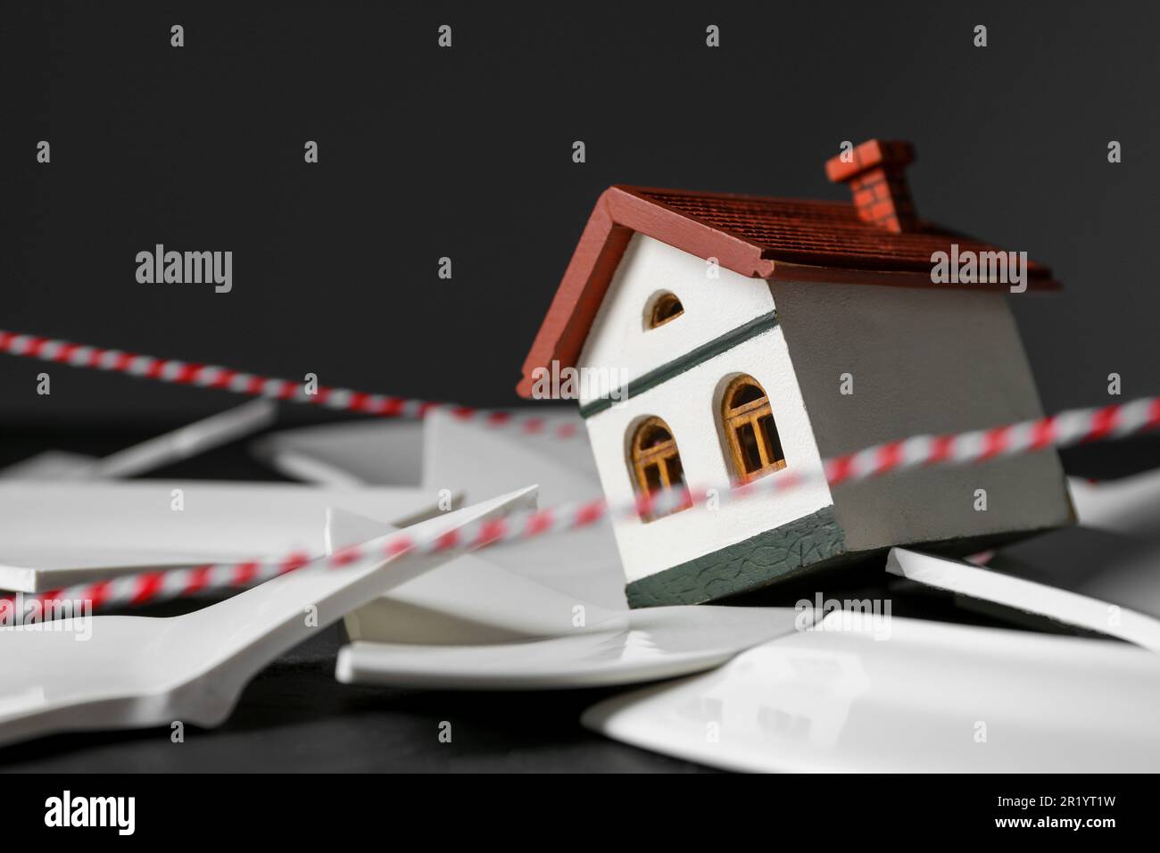 House model and broken dishes on black table depicting destruction ...