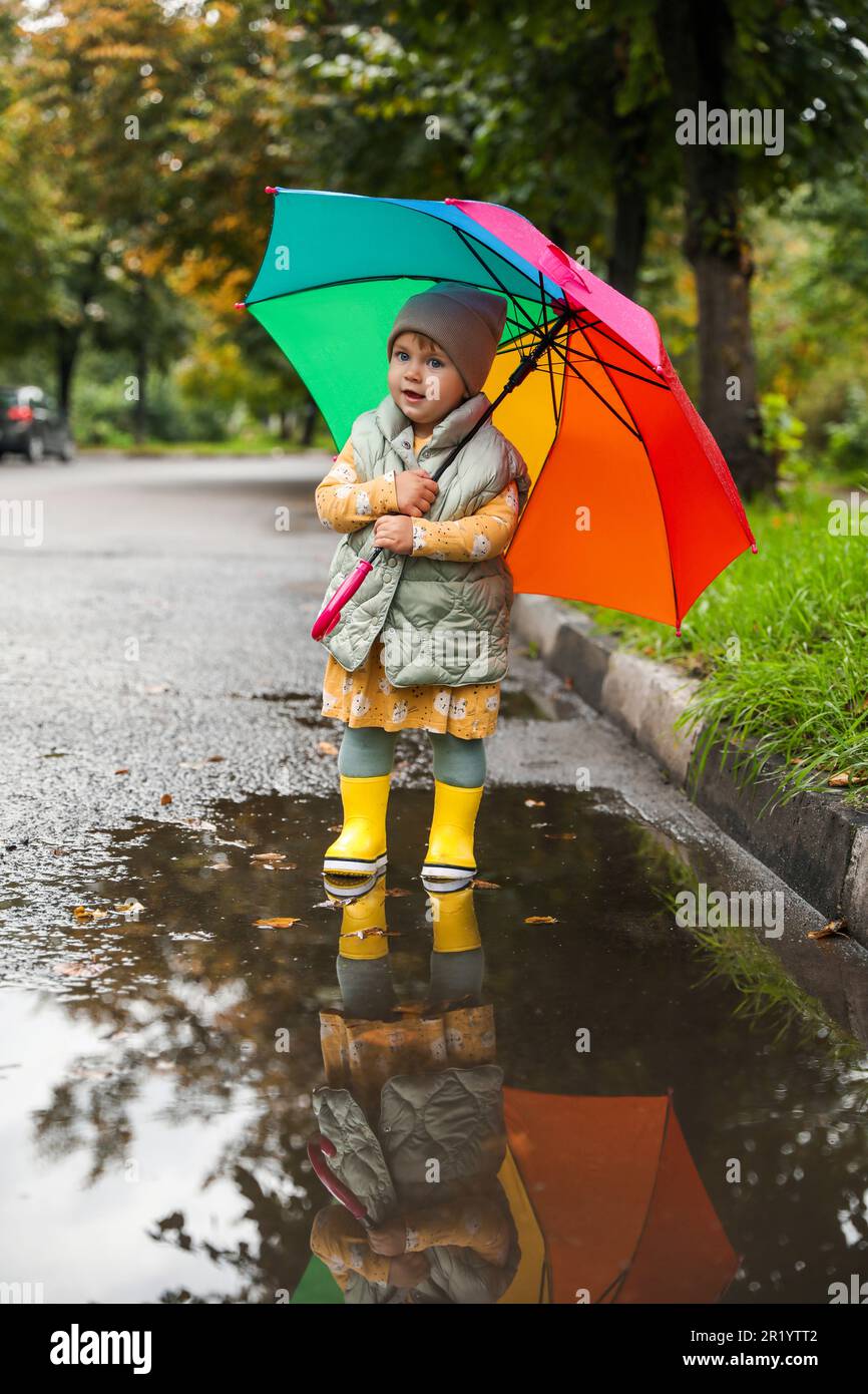 Cute little girl with colorful umbrella standing in puddle outdoors ...