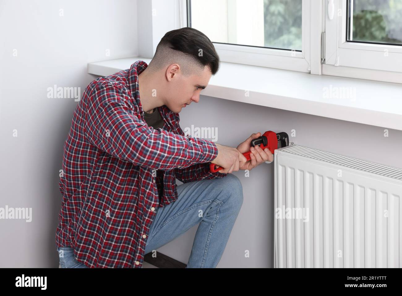 Man fixing radiator with pipe wrench in room Stock Photo - Alamy