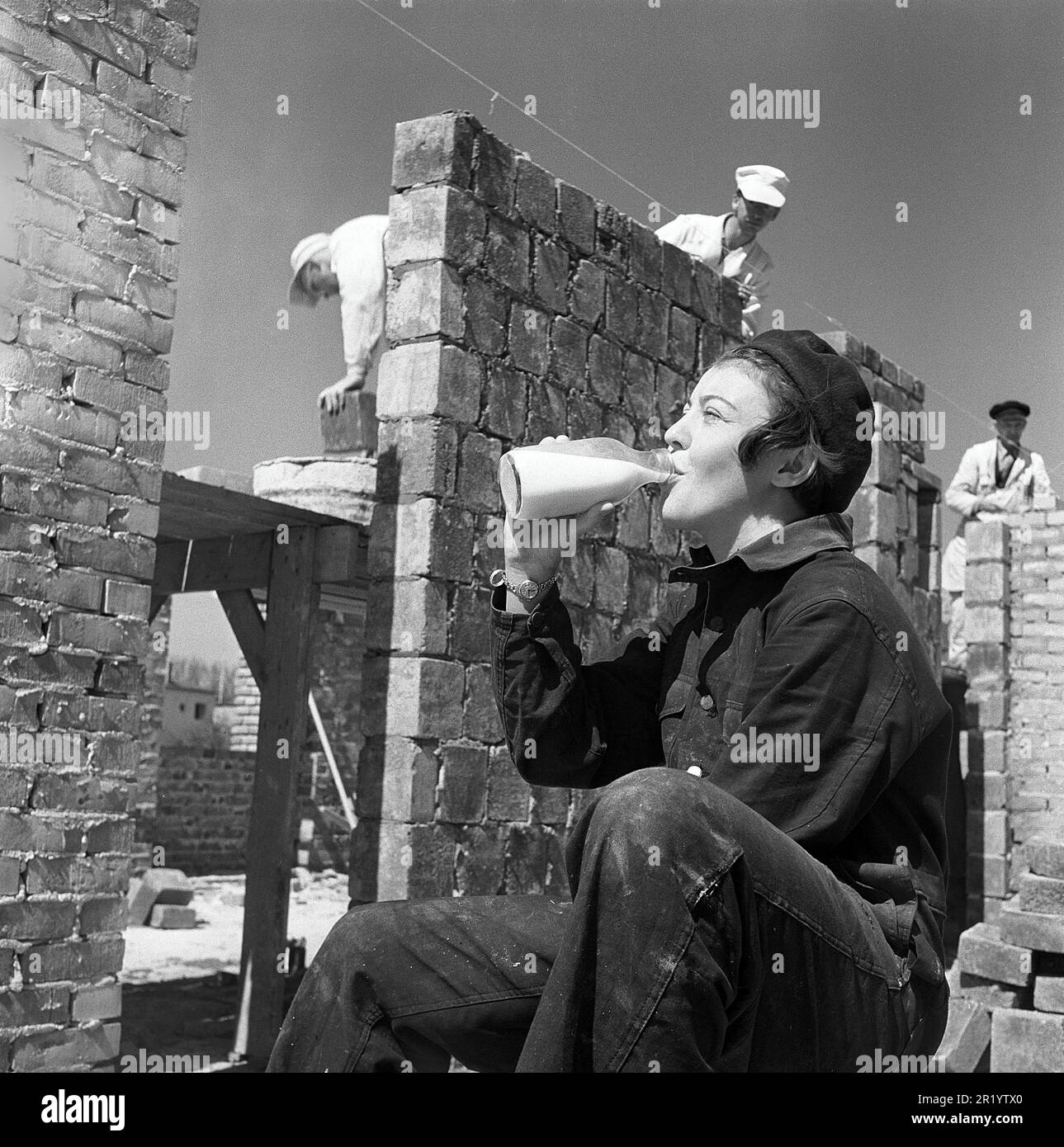 In the 1950s. A young female apprentice bricklayer drinks from a ...