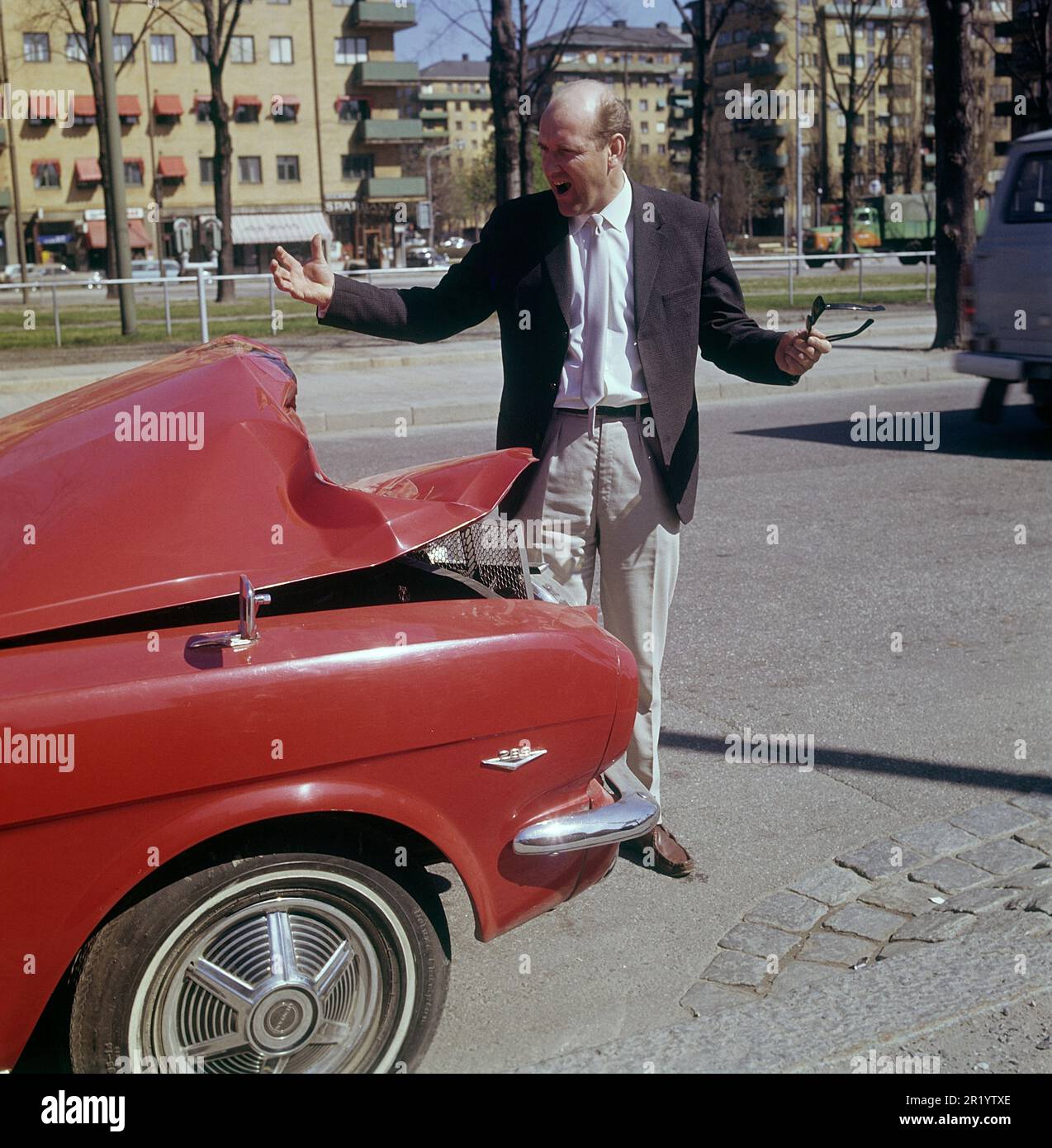Motoring in the 1960s. A man stands in front of his car that is visibly ...