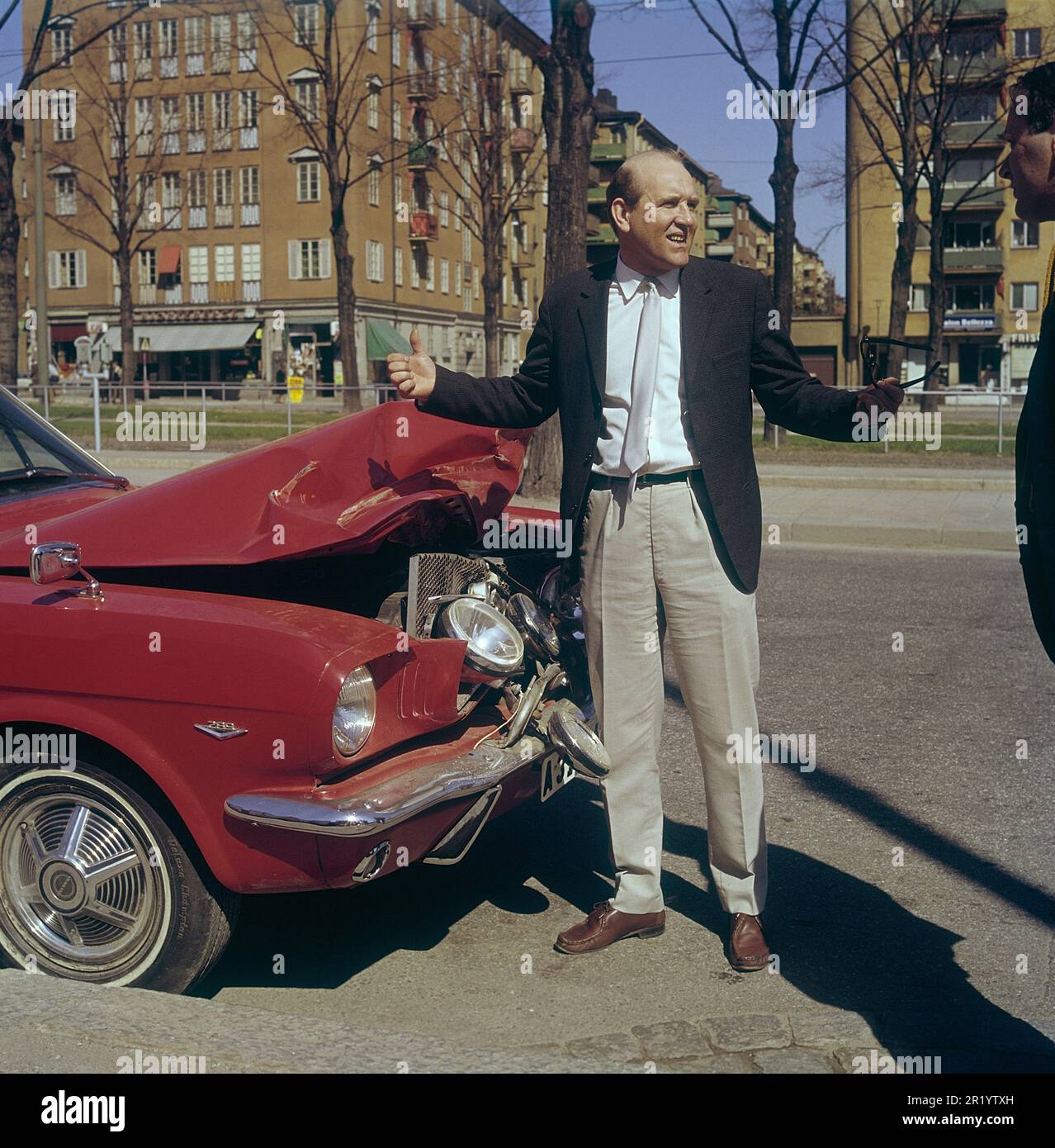 Motoring in the 1960s. A man stands in front of his car that is visibly ...