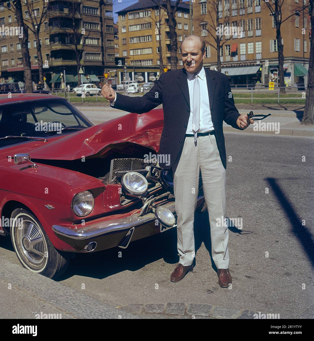 Motoring in the 1960s. A man stands in front of his car that is visibly ...