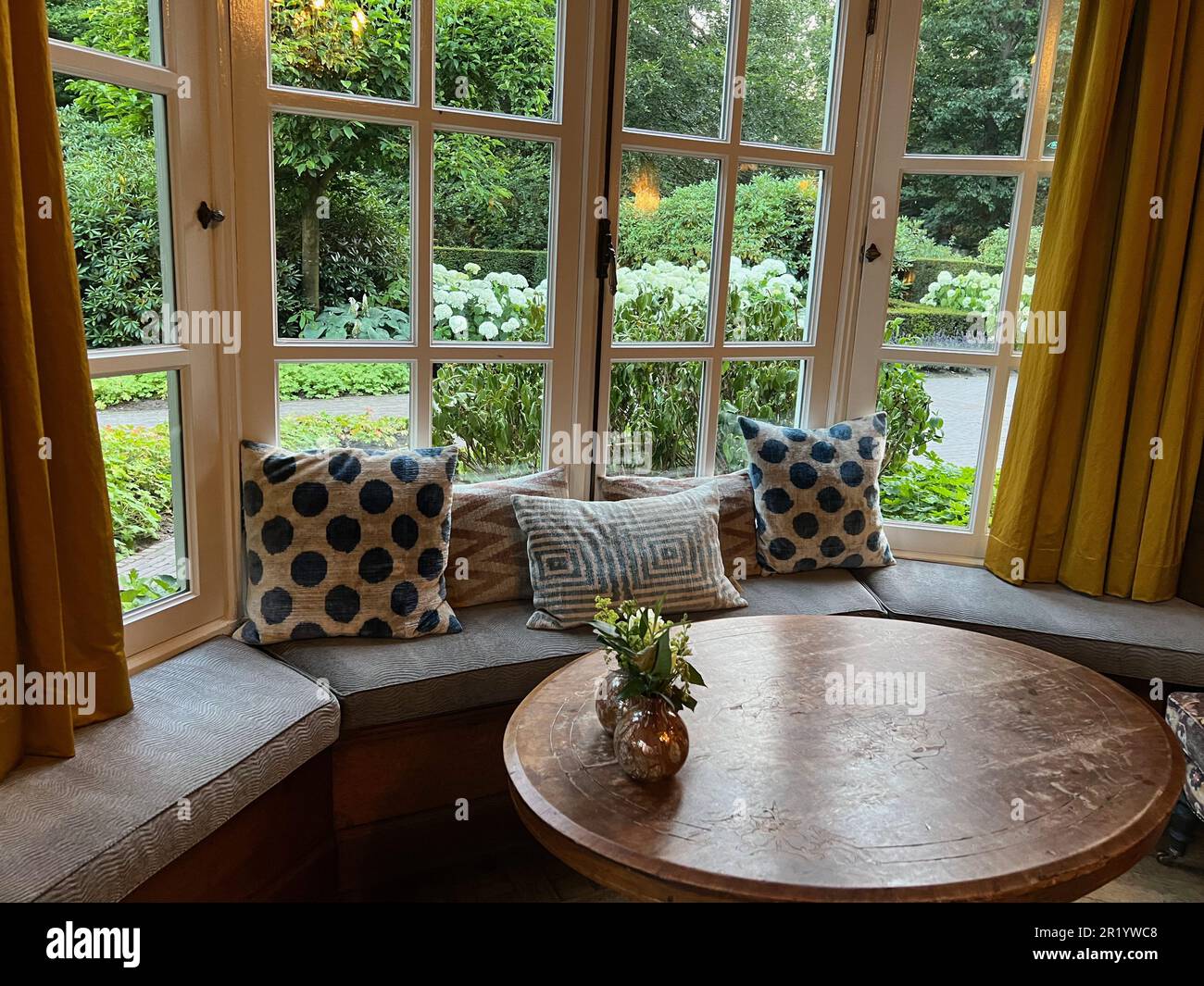 Wooden table near bay window seat with cushions in cozy room. Interior ...
