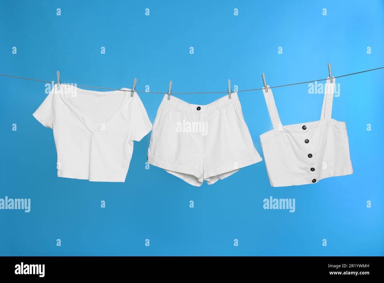 Different clothes drying on laundry line against light blue background ...