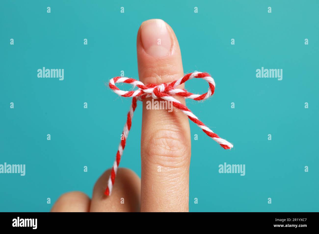 Woman showing index finger with tied bow as reminder on light blue ...