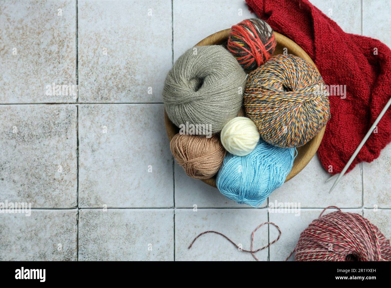 Soft woolen yarns, knitting and needles on grey tiled background, flat ...
