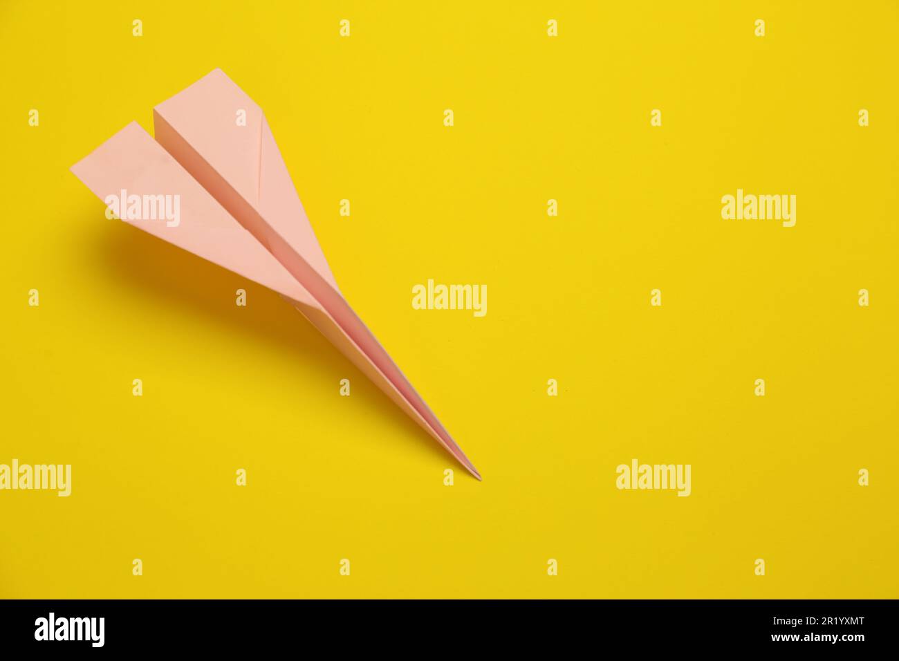 Handmade light pink paper plane on yellow background, above view. Space ...