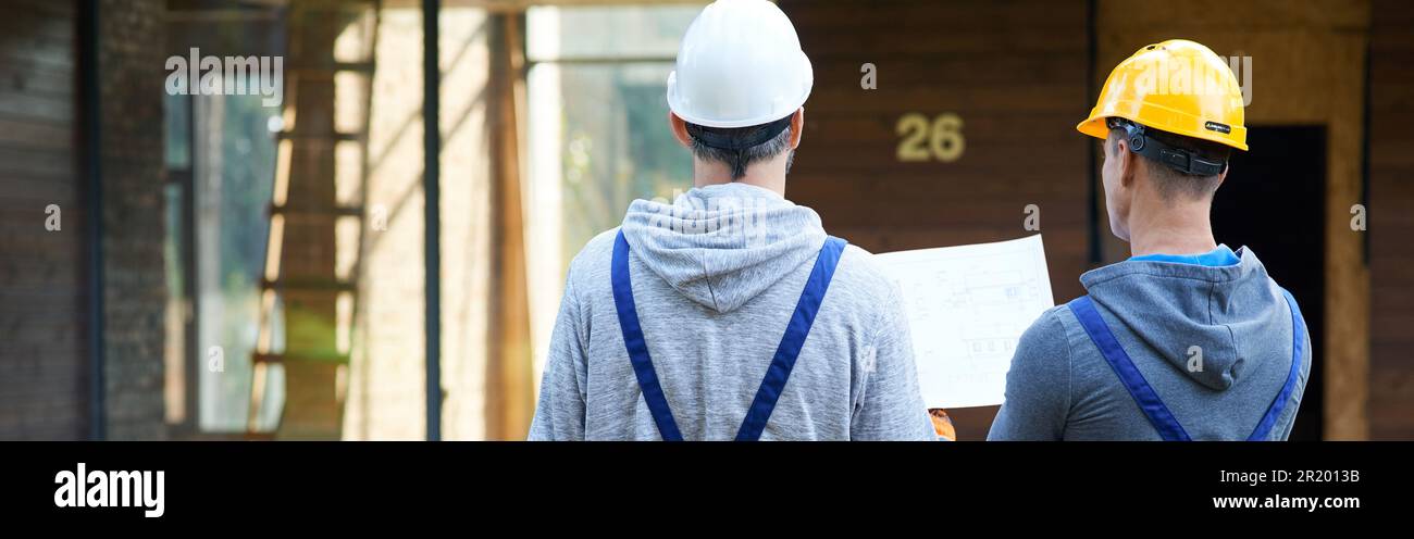 Plan it. Rear view of two builders standing outdoors with an open ...