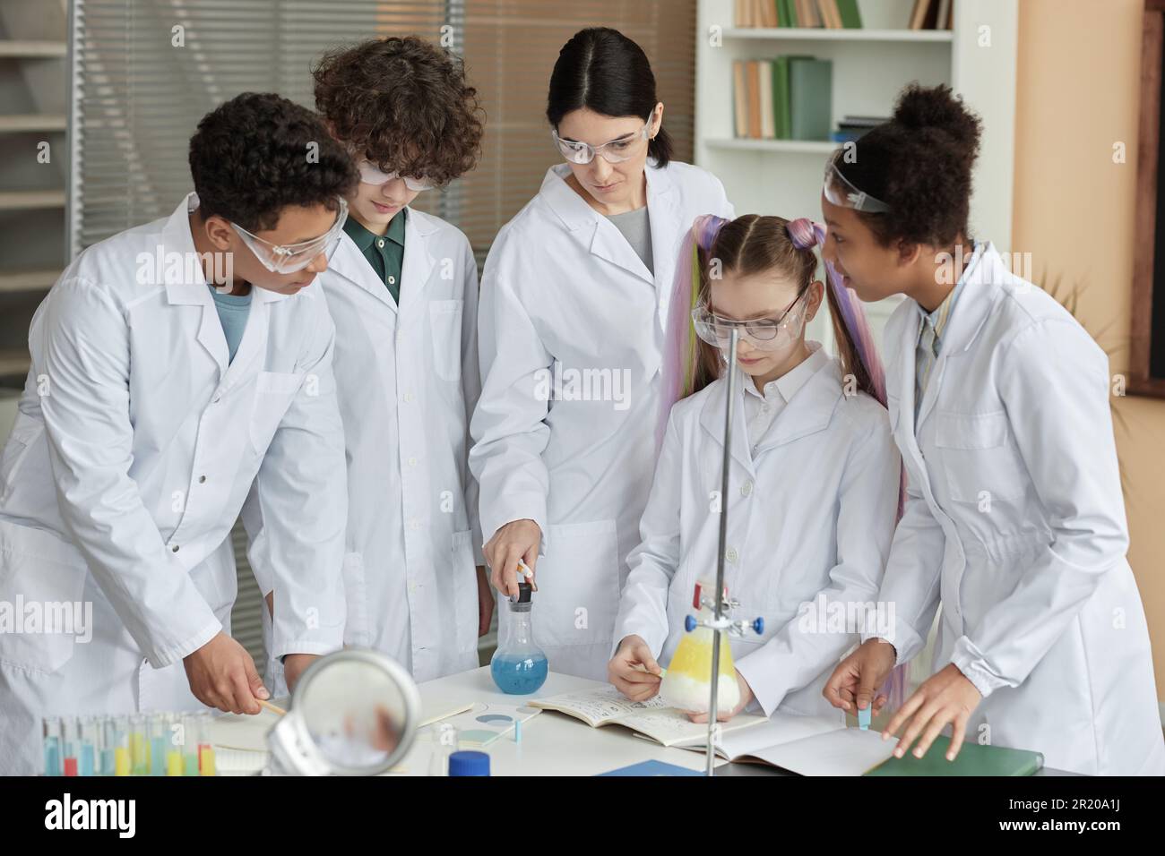 Diverse group of young teens wearing lab coats doing science ...