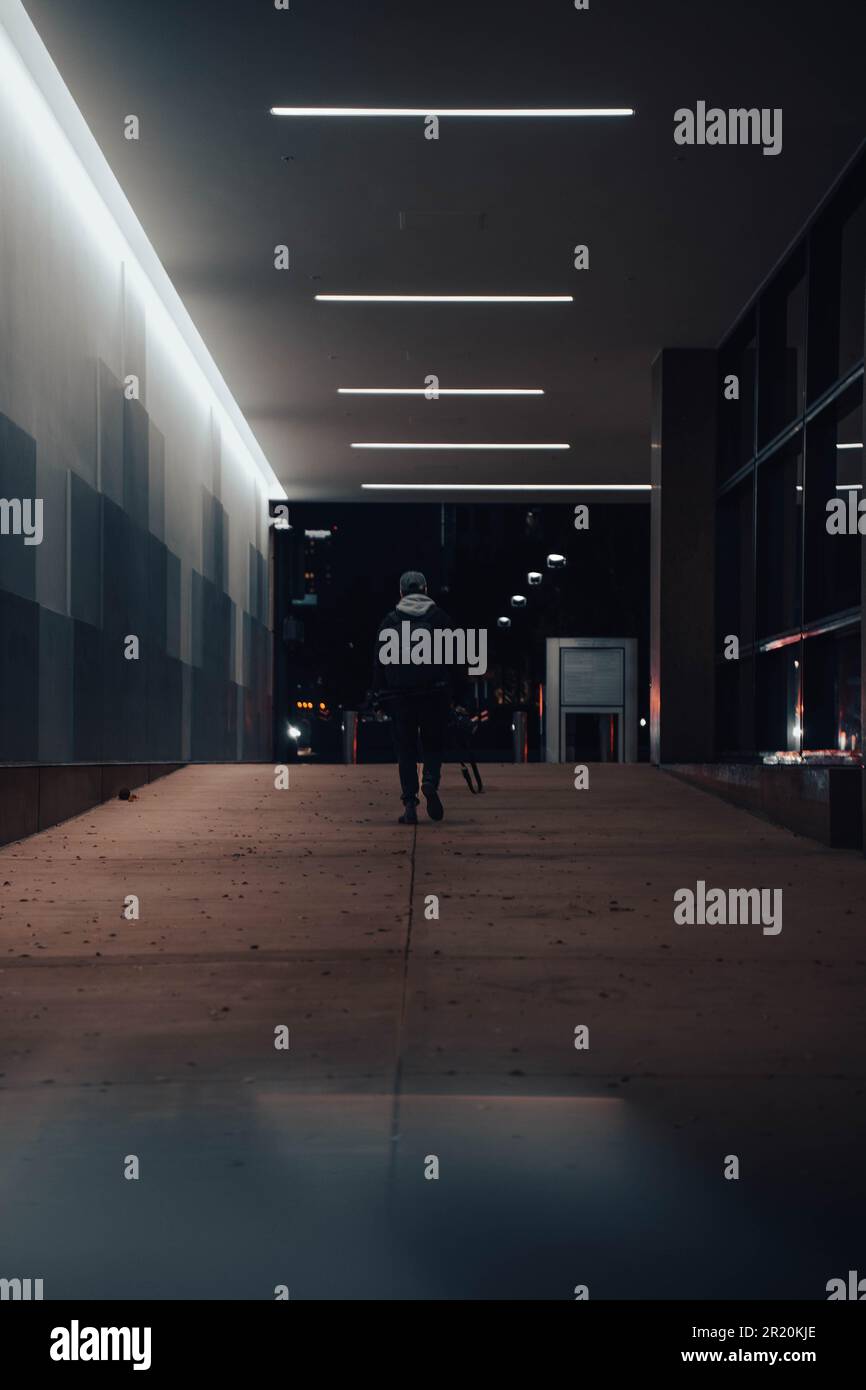 A young woman confidently strides through a dimly lit hallway ...