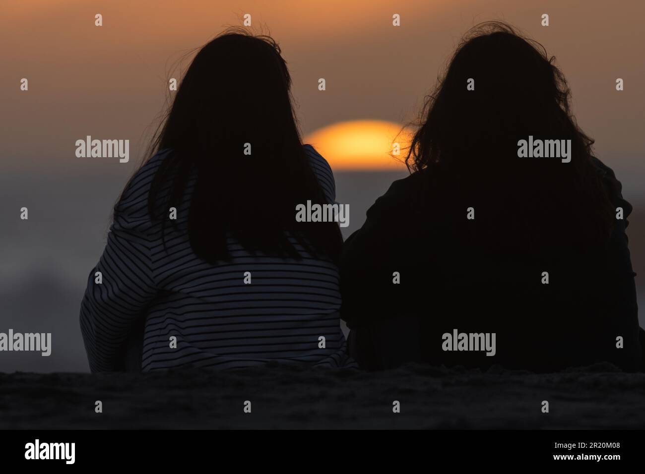 Two girls sitting and watching the sunset Stock Photo - Alamy