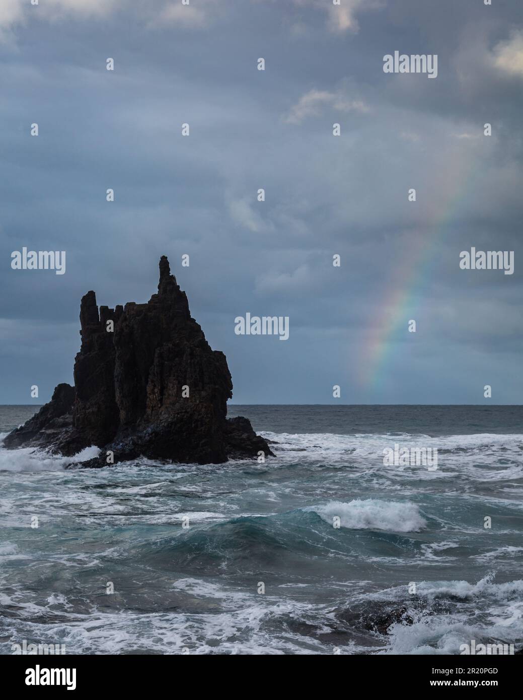 A beautiful rainbow arches over a tranquil ocean landscape with jagged ...