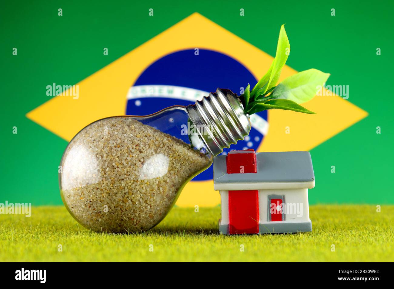 Plant growing inside the light bulb, miniature house on the grass and ...