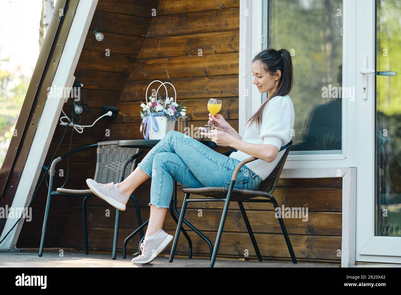Woman enjoys warm weather sitting on terrace of wooden cabin with ...