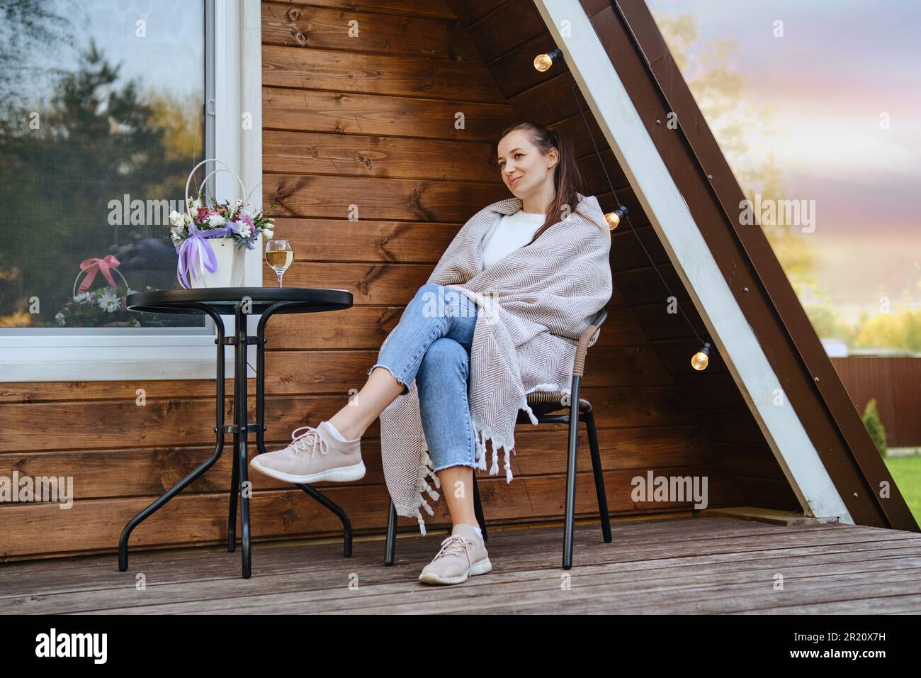 On warm evening, woman wraps herself in cozy blanket and rests on ...