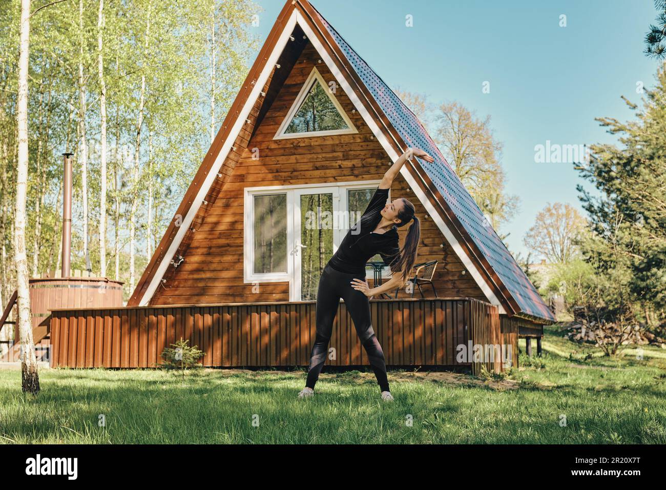 Active woman bends body to the sides during workout on lawn of her a ...