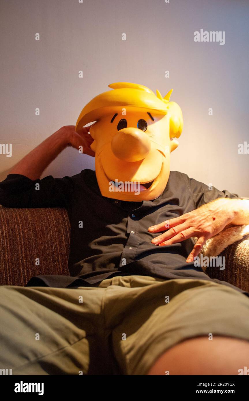A mature adult with a mask of Barney Rubble on the sofa Stock Photo - Alamy