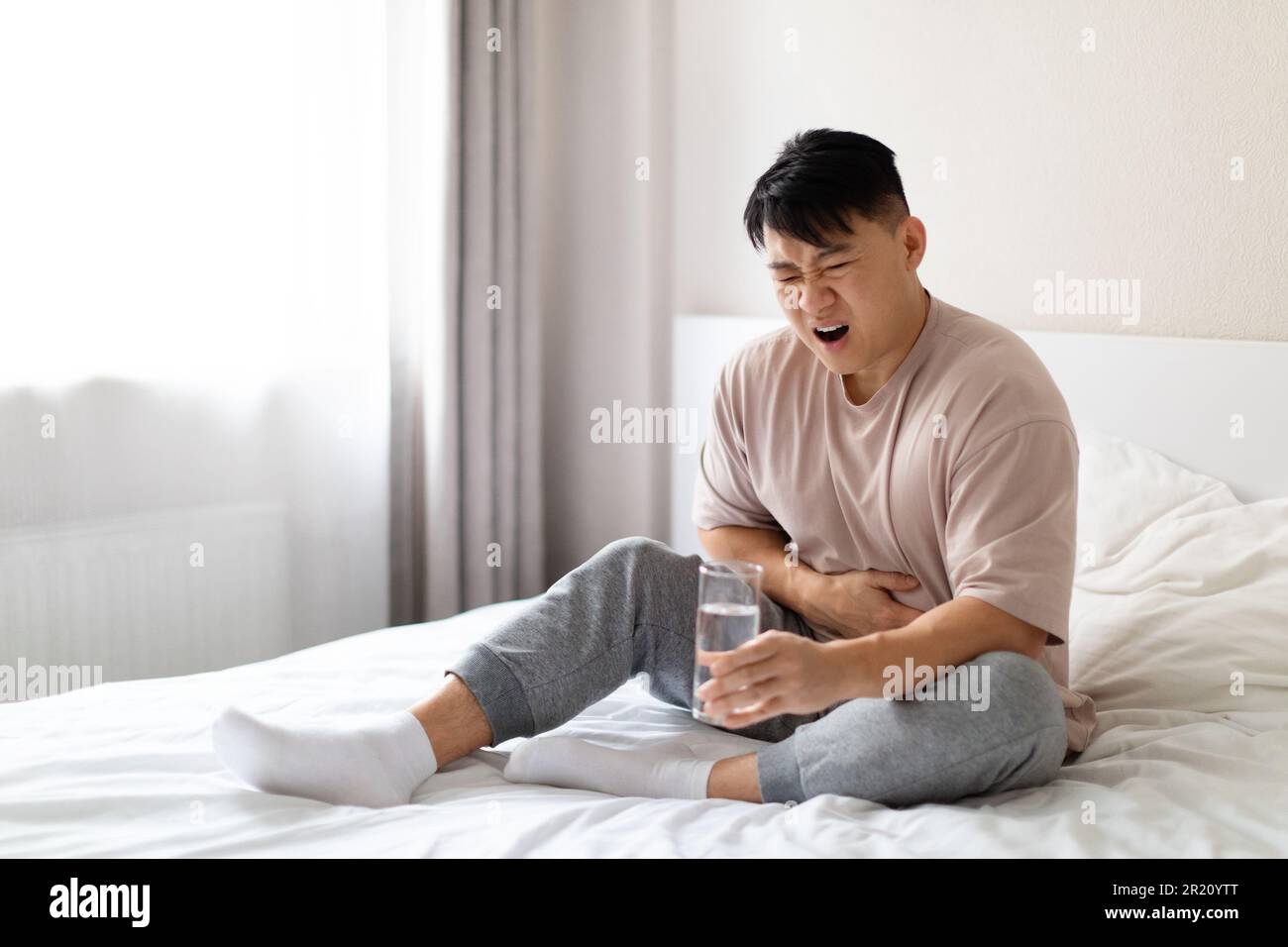 Chinese man sitting on bed, suffering from stomach pain Stock Photo - Alamy