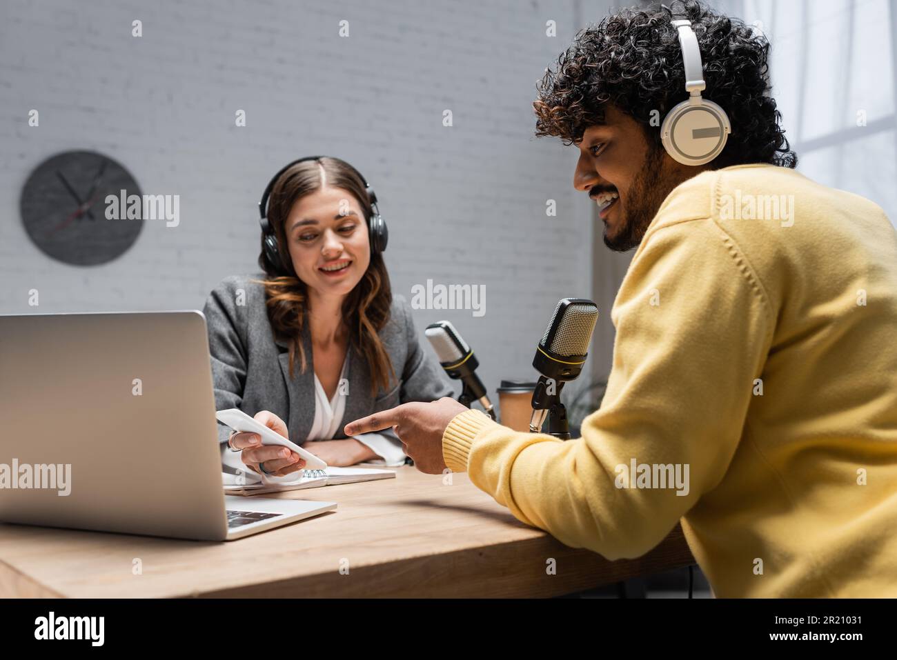 charming radio host in grey blazer showing smartphone to young indian ...