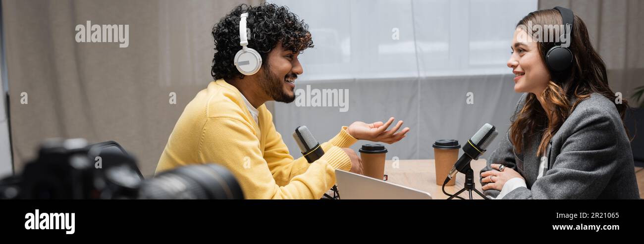 side view of happy indian man in headphones and yellow jumper gesturing ...