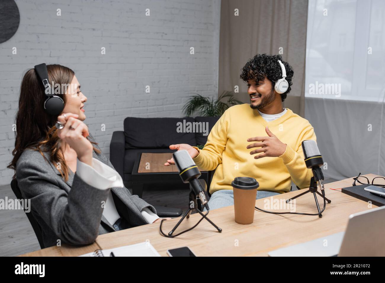 happy multiethnic radio hosts in headphones talking near professional ...