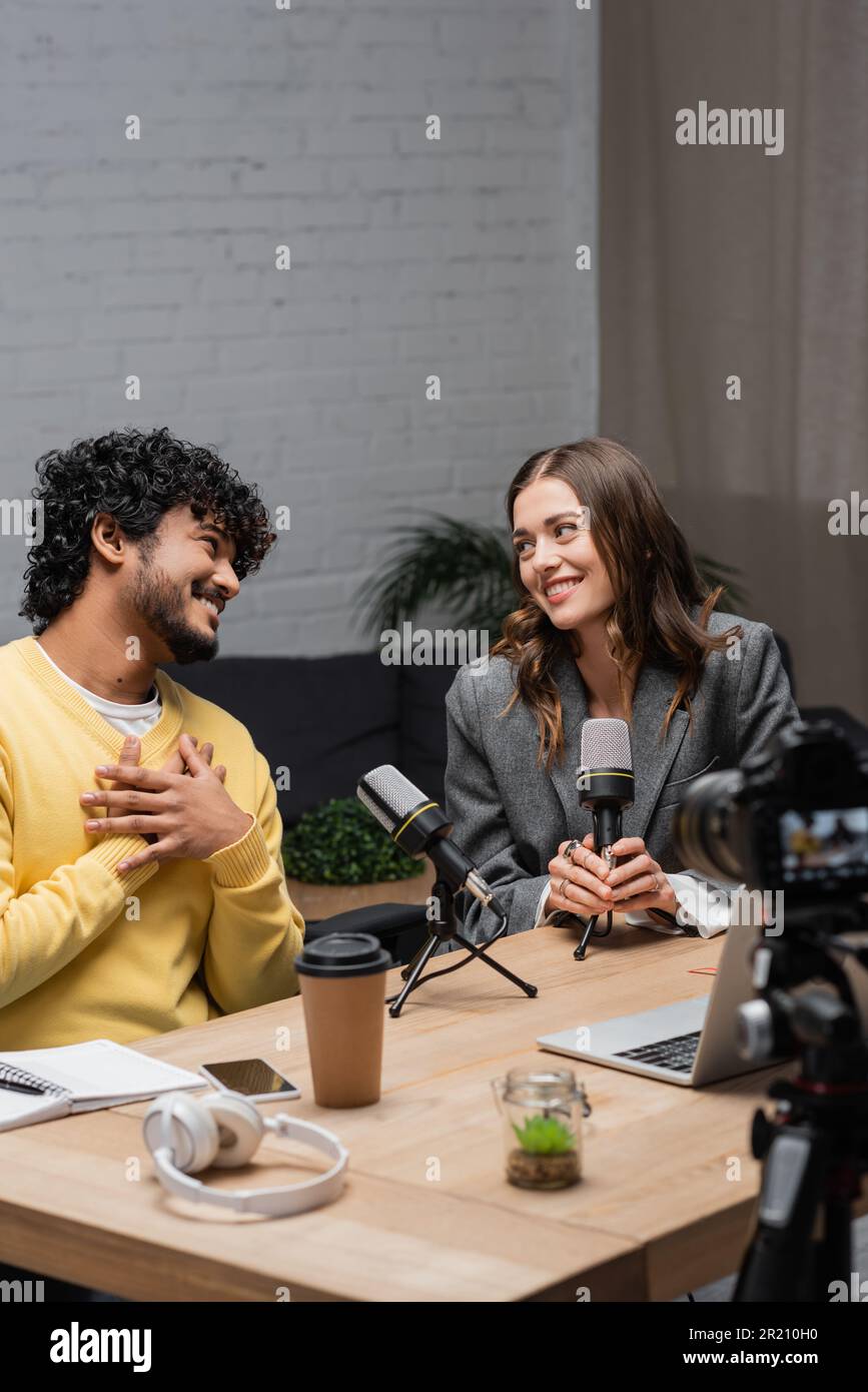 pleased indian radio host talking to smiling colleague near microphones ...