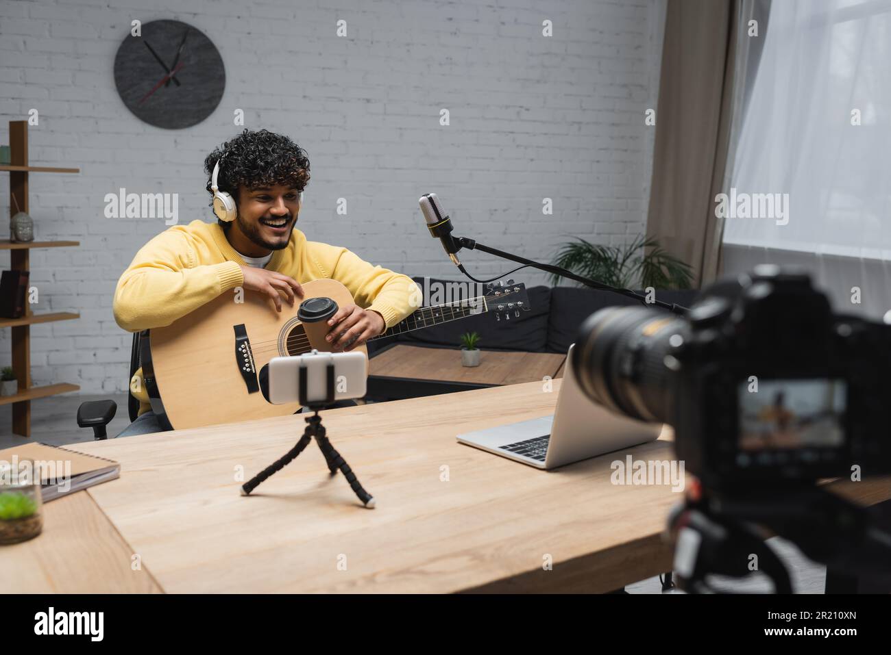 Smiling indian podcaster in headphones holding acoustic guitar and ...