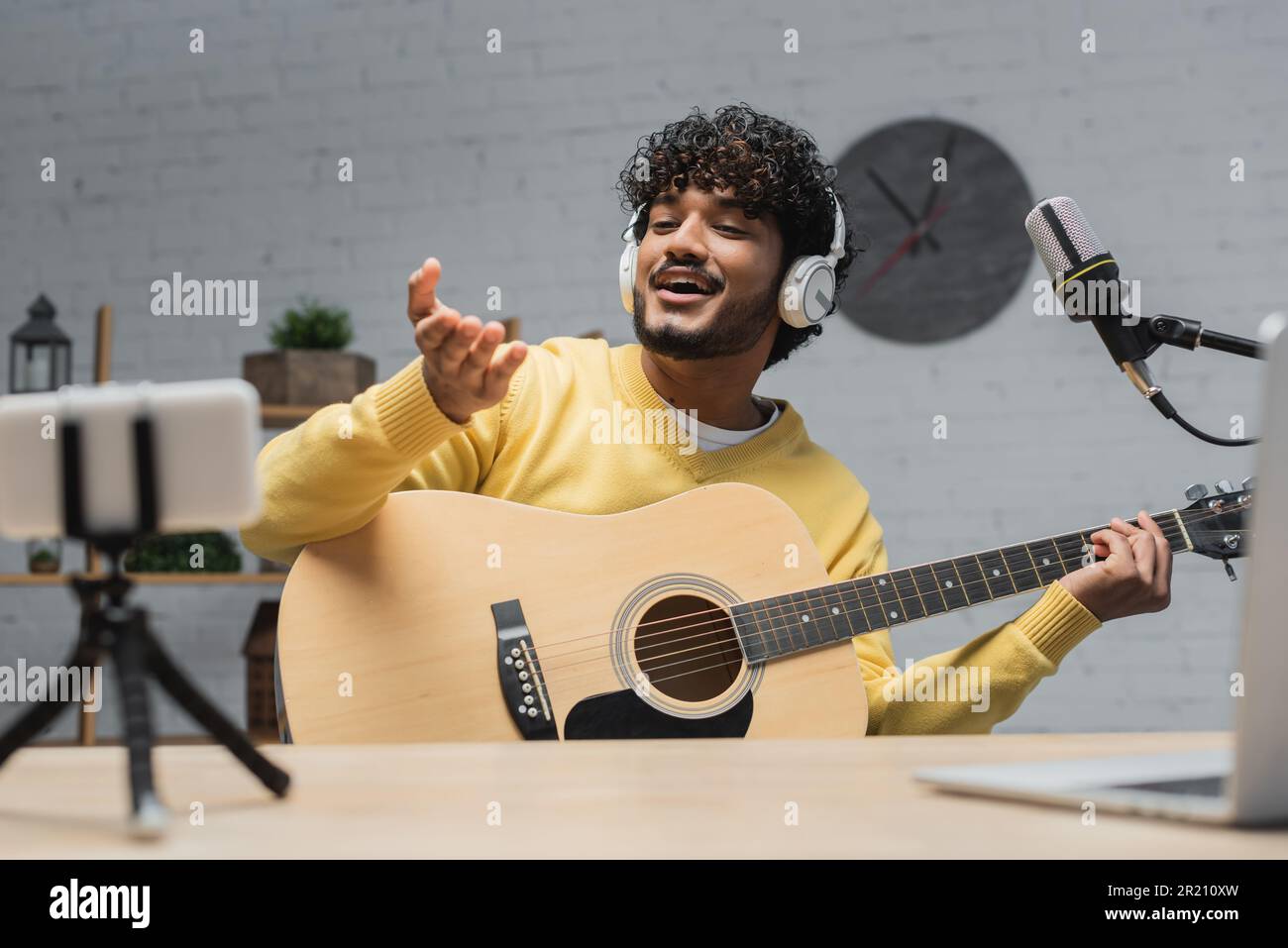 happy and curly indian podcaster in headphones and yellow jumper ...