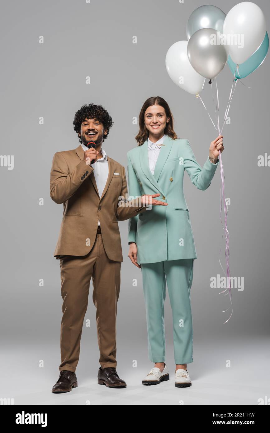 Full length of smiling young indian event host talking at microphone ...