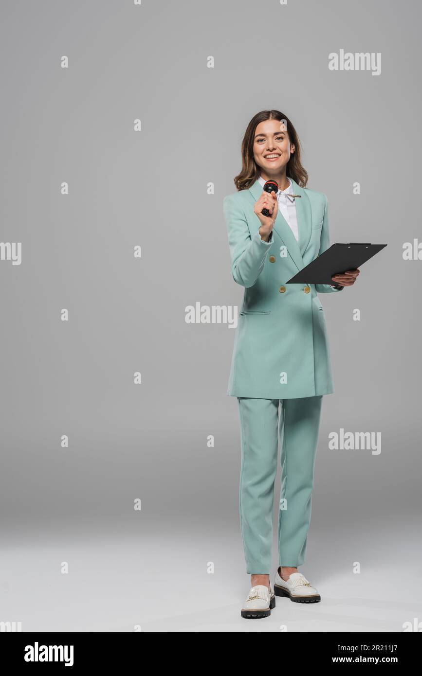Full length of smiling and brunette event host in blue suit holding ...