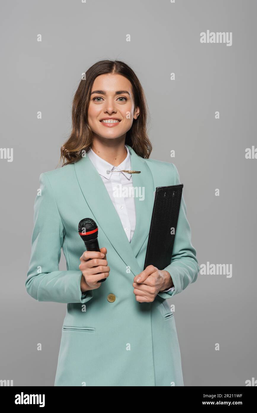 Portrait of positive brunette host of event in blue suit holding ...