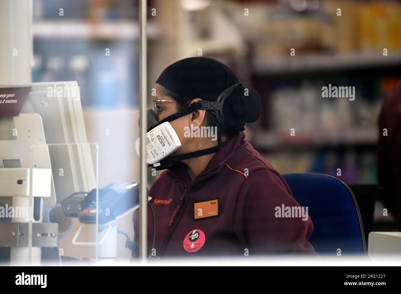 Photograph of a supermarket worker wearing a face covering during the ...