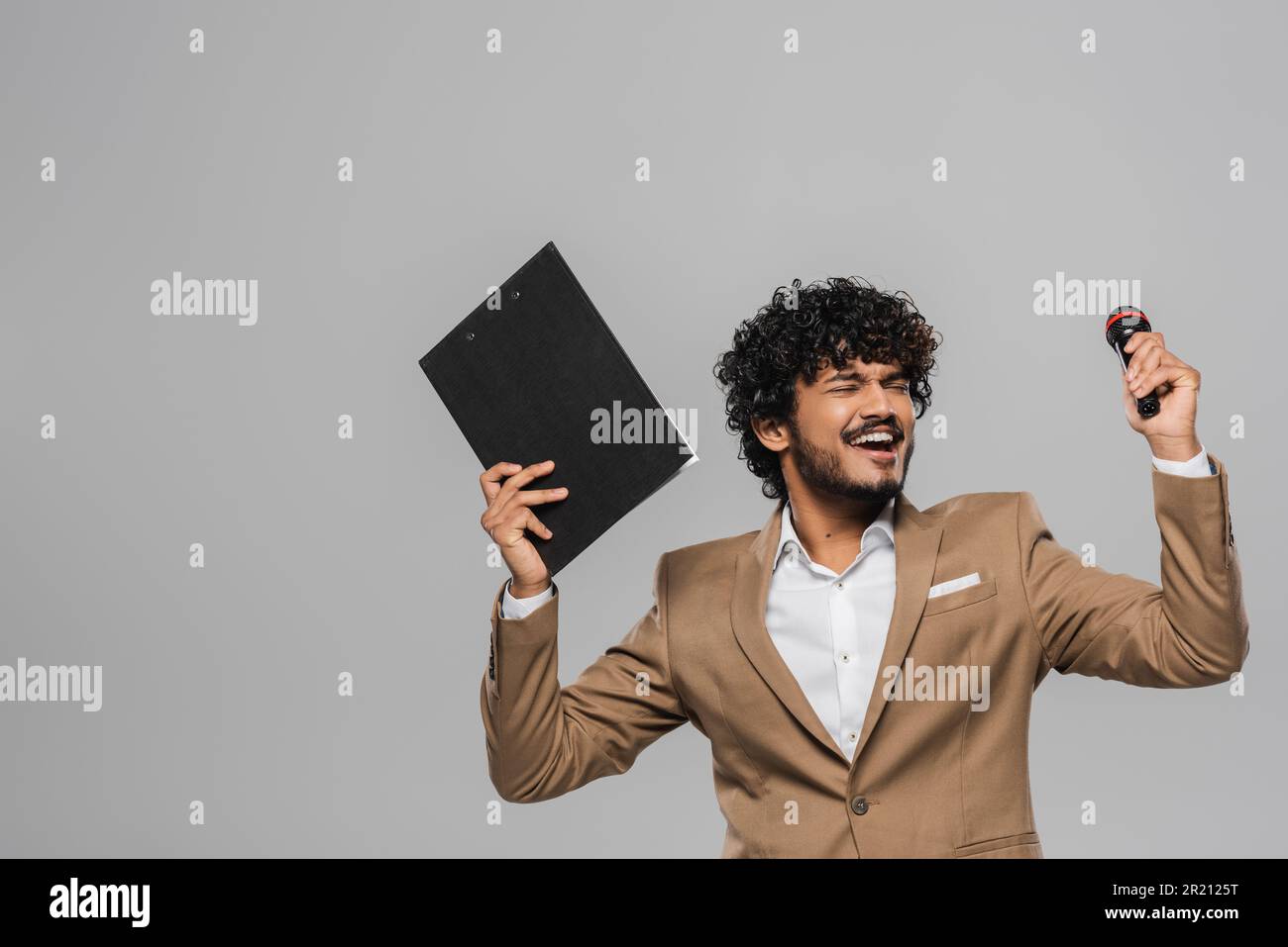 Excited young indian event host with curly hair in formal wear closing ...
