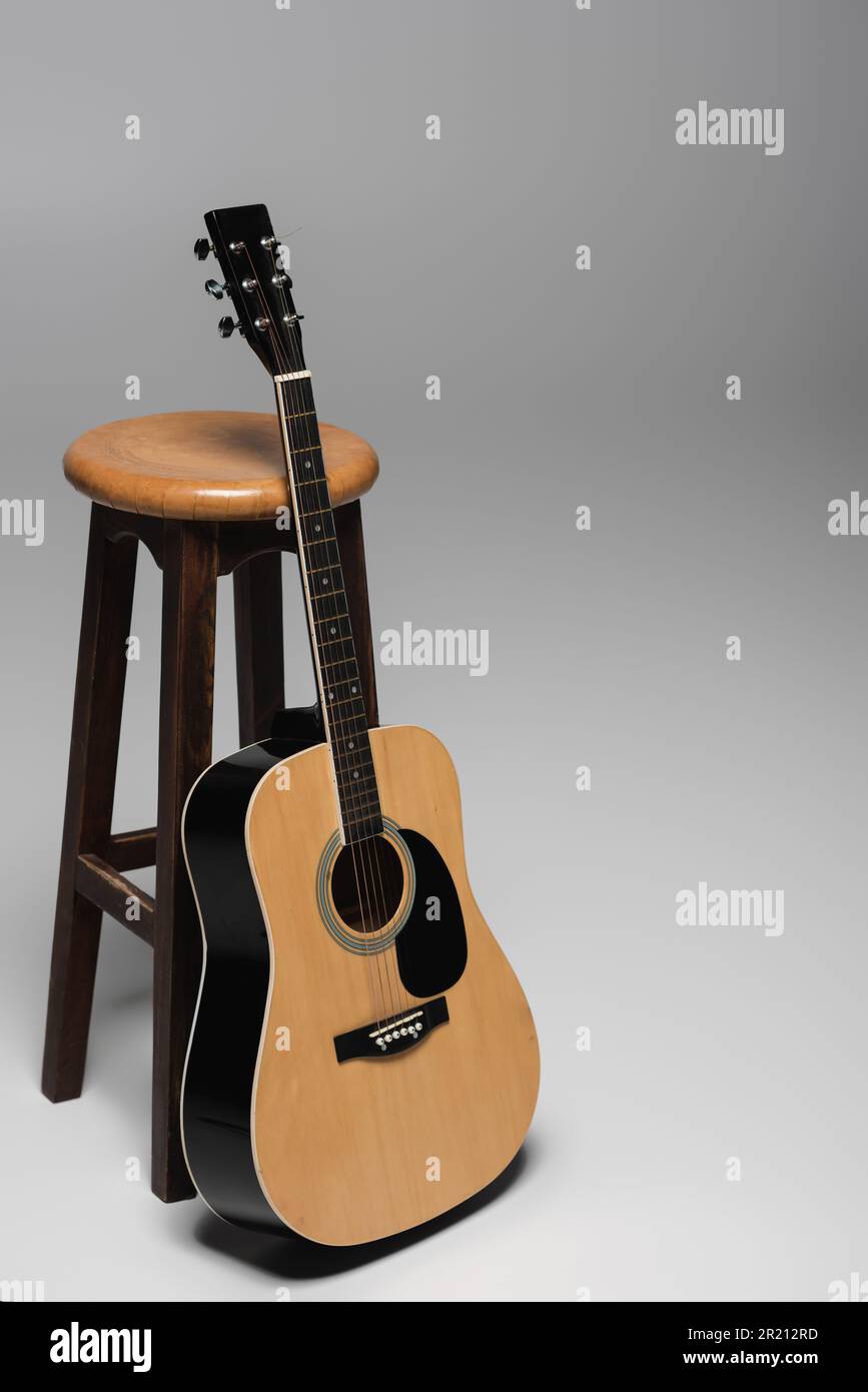 Acoustic guitar standing near brown wooden chair on grey background ...
