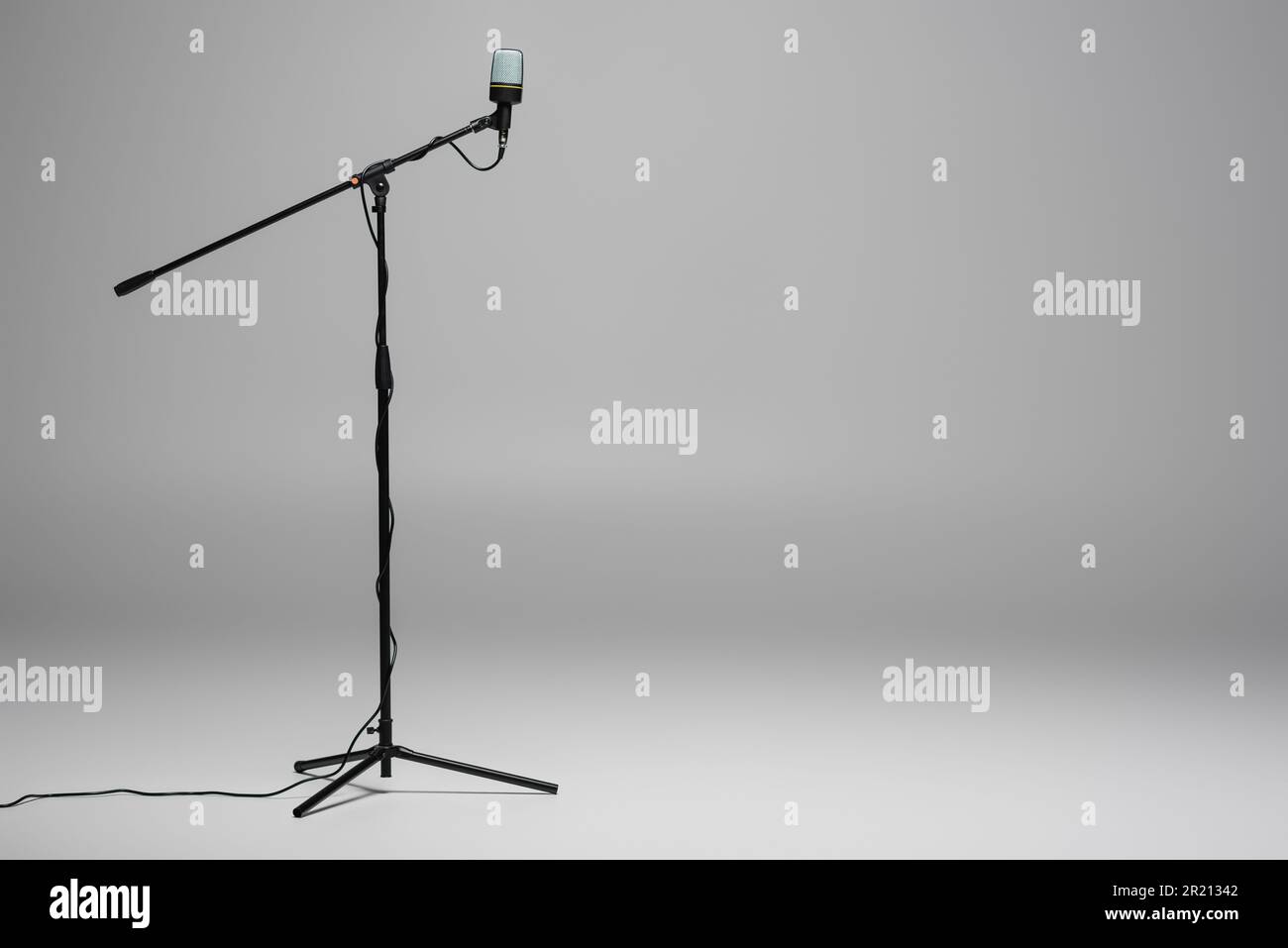 Black microphone with wire on metal stand on grey background with copy ...