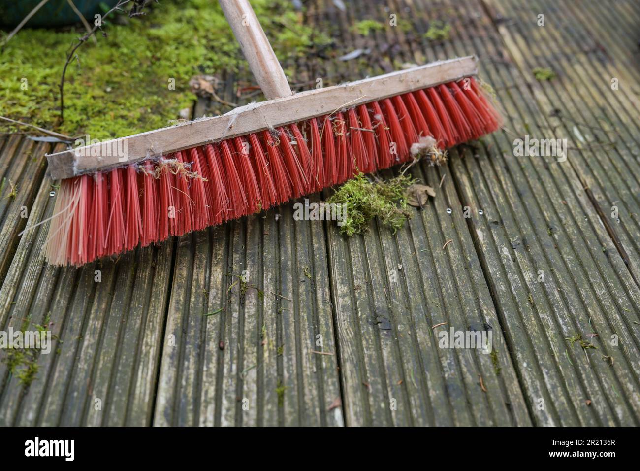 Outdoor broom with red plastic bristles on a weathered wooden deck with ...