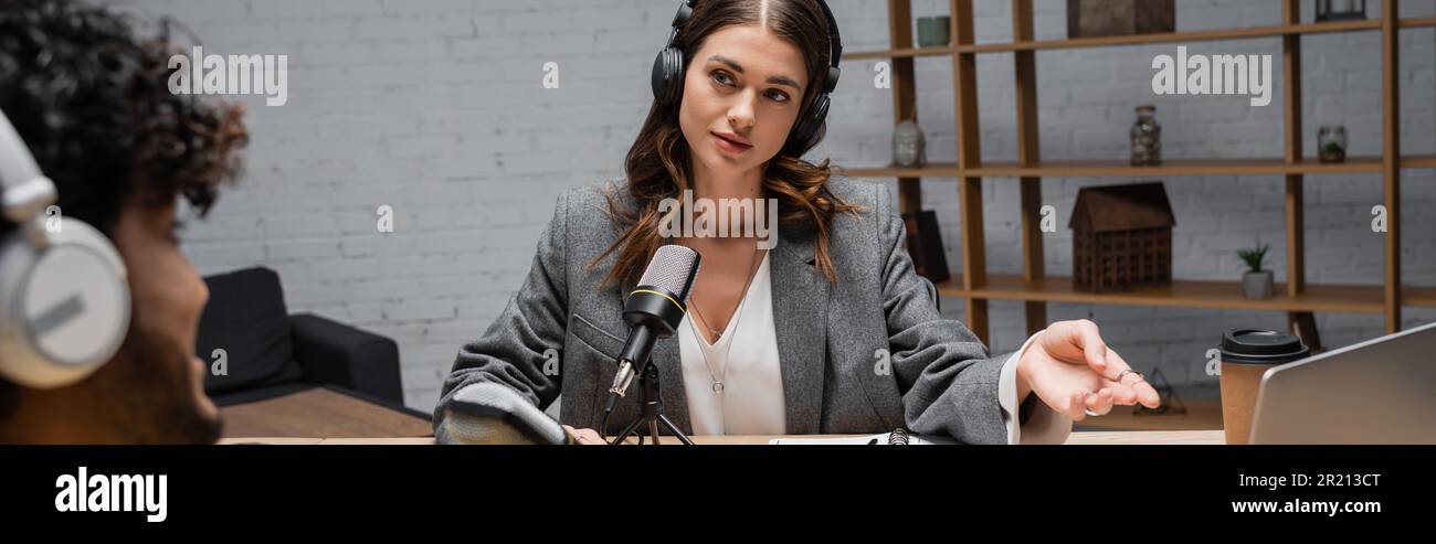 charming radio host in headphones and grey blazer pointing at laptop ...