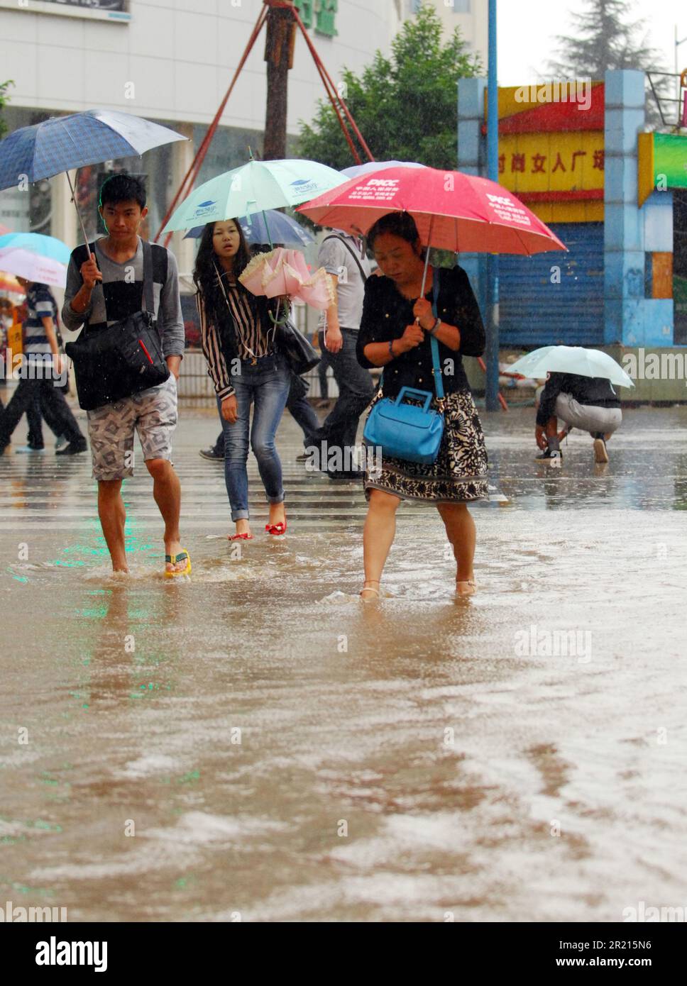 Pedestrians walk across a flooded street in heavy rain in Kunming ...