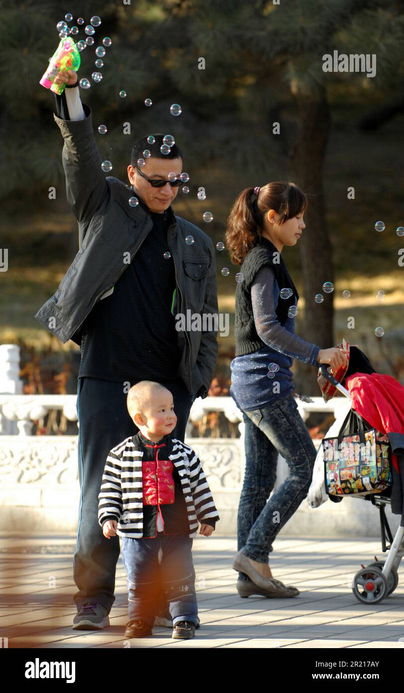 A father entertains his child by blowing bubbles in Taoranting Park ...