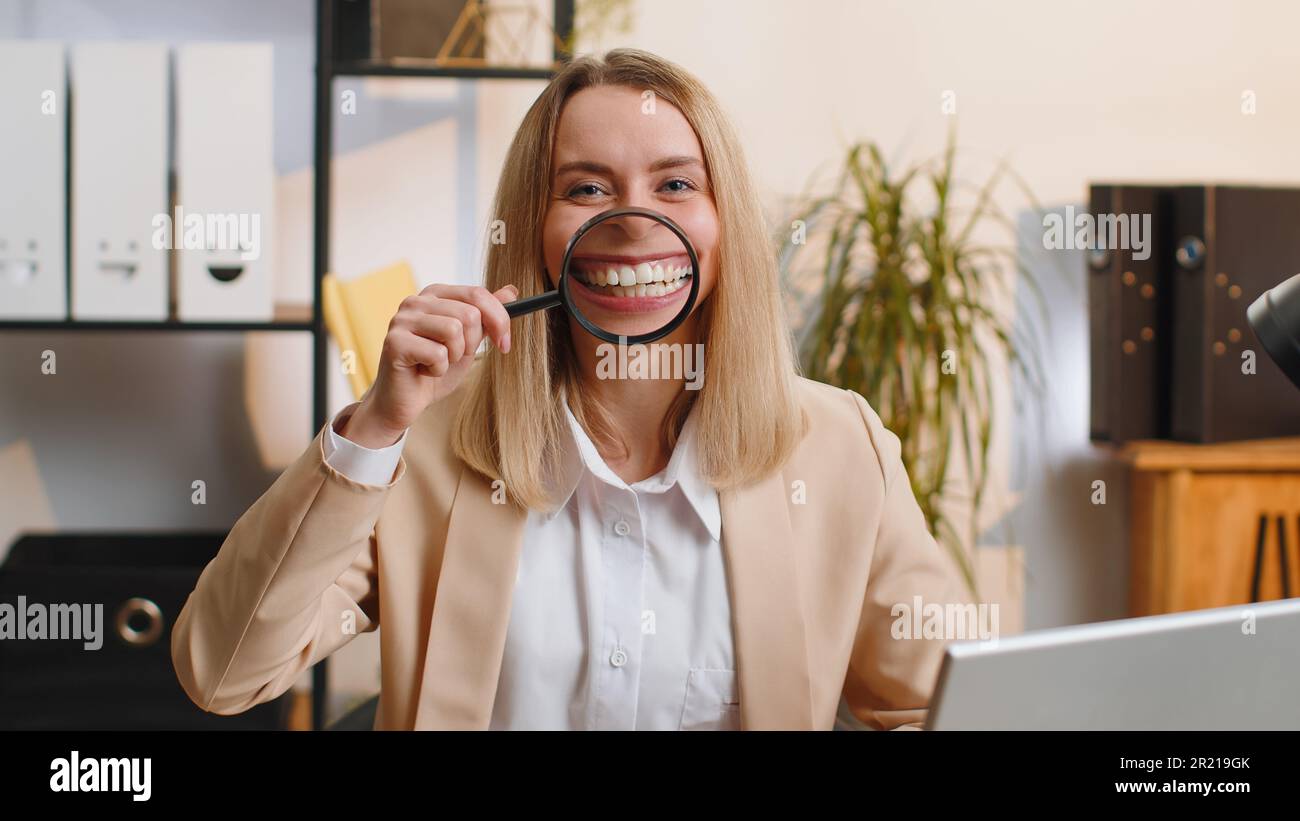 Businesswoman holding magnifier glass on teeth, looking at camera with ...
